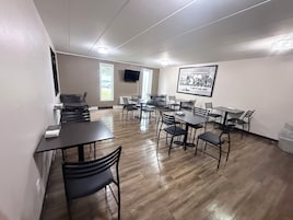 Sala de conferências com várias mesas e cadeiras, uma TV de tela plana na parede e um quadro com a imagem de um lago.