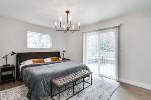 Quarto com uma cama grande, um banco, um candelabro e vista pela janela.