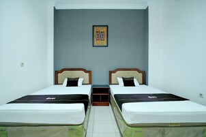 Quarto de hotel com duas camas de solteiro, uma pequena mesa, prateleira na parede e um quadro emoldurado.