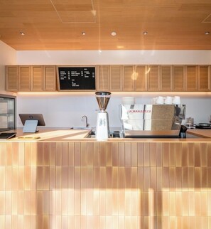 Uma área de recepção com balcão de madeira, painel de menu digital e máquina de café.