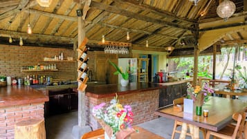 Um espaço de bar rústico com vigas de madeira, balcão de tijolos e diversos garrafas e copos.