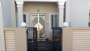 Entrada de um prédio com porta protegida por grades, tapete verde e um pequeno degrau que leva à porta.