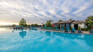 Piscina com espreguiçadeiras e um edifício com porta e janelas.