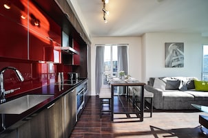 Uma cozinha moderna com painel de parede vermelho, um espaço de refeições com um banco e uma sala de estar com sofá e um quadro na parede.
