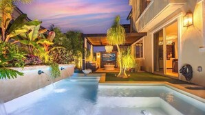 Uma área moderna de piscina externa com hidromassagem, cercada por vegetação exuberante e um céu ao pôr do sol.