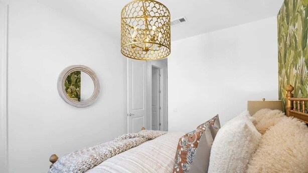 Um quarto com uma cama, um espelho redondo, uma porta e uma luminária fixada na parede.