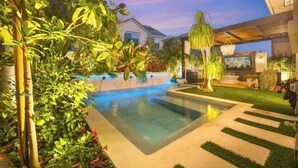 Uma área de piscina moderna ao ar livre, com piscina cristalina, rodeada por vegetação e um gramado bem cuidado.