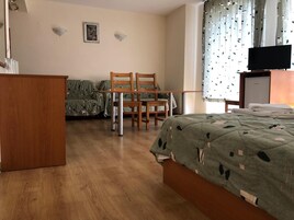 Quarto de hotel com cama, secretária de madeira, cadeira, televisão e janela com cortinas.