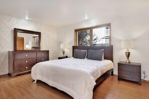 Quarto com cama, duas mesas de cabeceira, cômoda, janela e espelho.