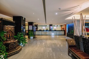 Um saguão de hotel com balcão de recepção, uma fonte decorativa e uma área de estar.