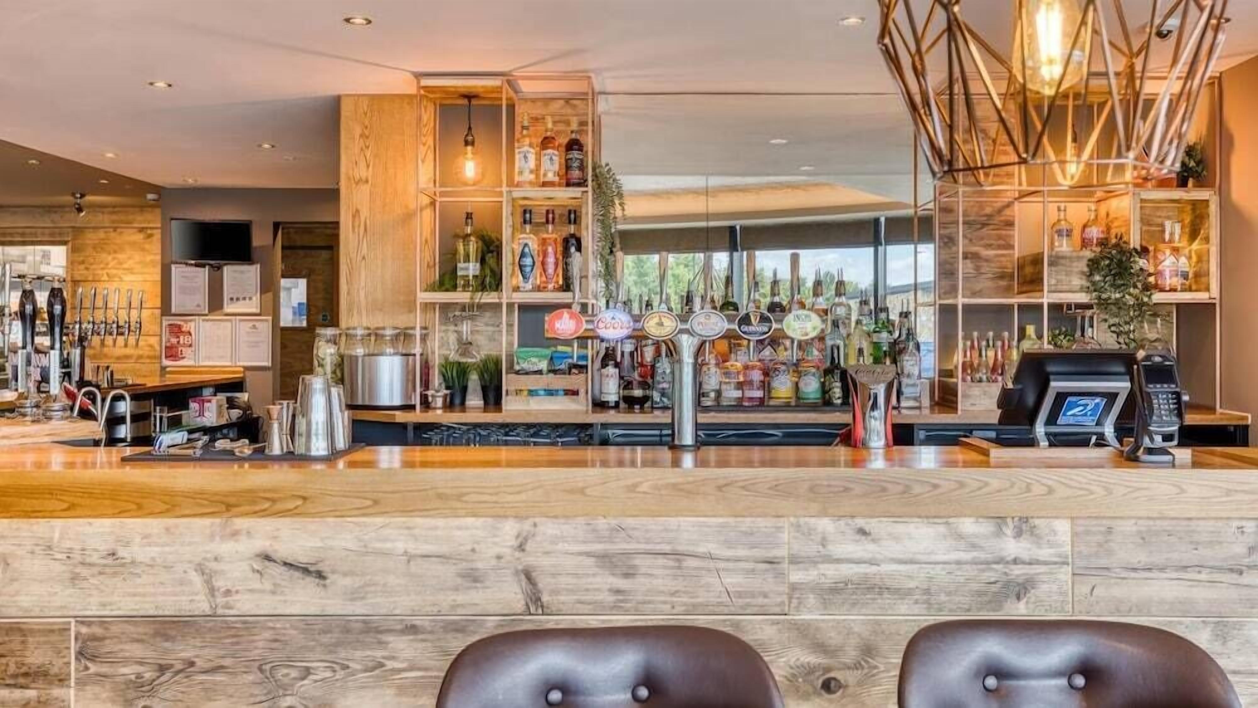 Uma área de bar com balcão de madeira, várias torneiras e uma seleção variada de garrafas.