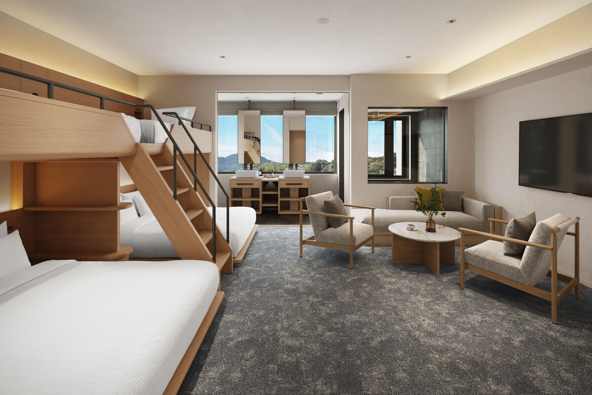 Quarto de hotel moderno com cama, sofá, mesa de centro e vista para o exterior.