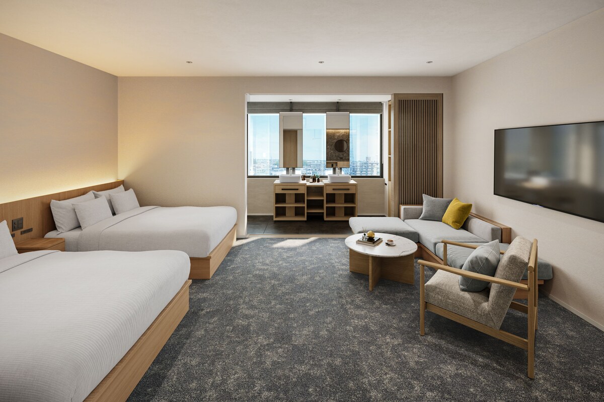 Quarto de hotel com duas camas, um sofá, uma mesa de centro, uma televisão e um banheiro com pia e espelho.