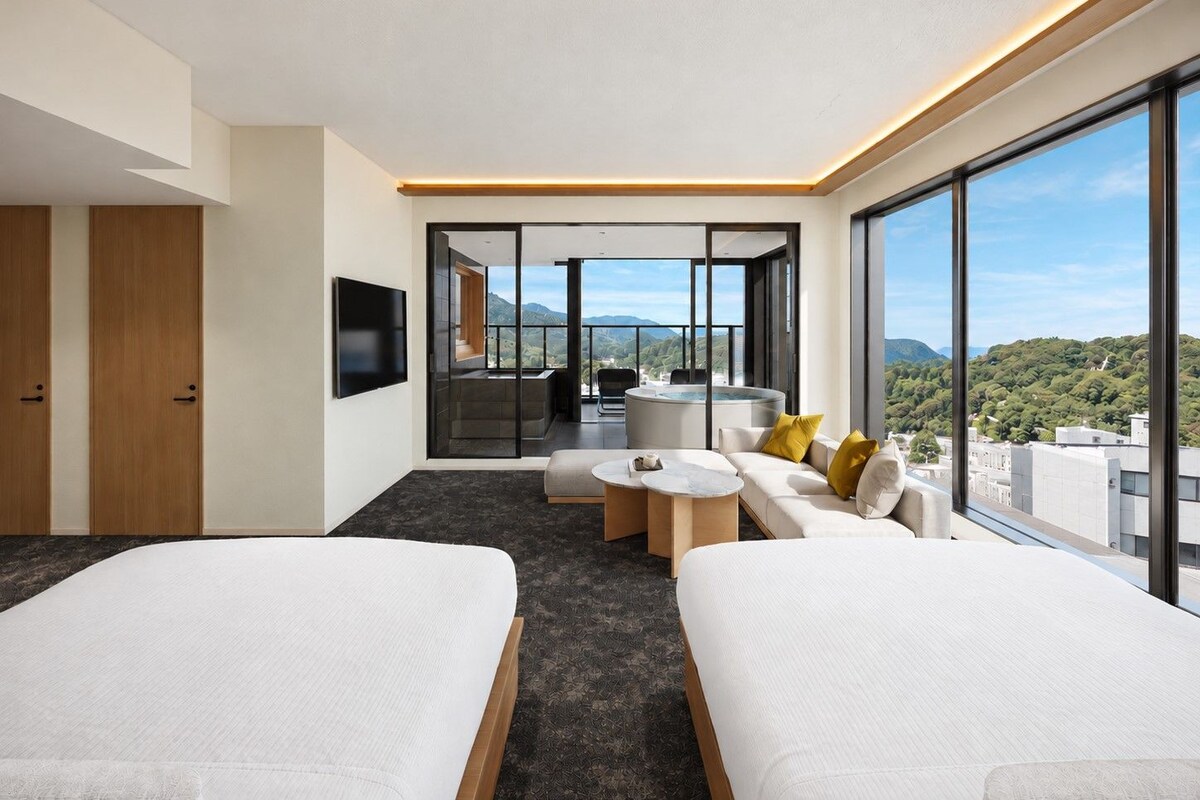 Quarto de hotel moderno com duas camas, um sofá, uma mesa de centro e varanda com hidromassagem.