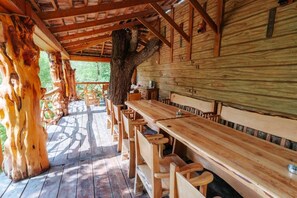 Uma cabana de madeira com uma mesa de jantar comprida e bancos, cercada por árvores altas.