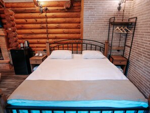 Uma cama de casal com cabeceira de madeira, uma mesa de cabeceira com chaleira e um cabideiro.