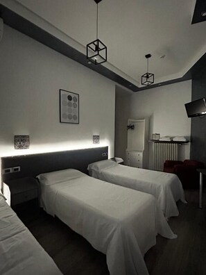 Quarto de hotel com duas camas de solteiro, uma mesa de cabeceira, uma cadeira, uma escrivaninha e uma televisão.