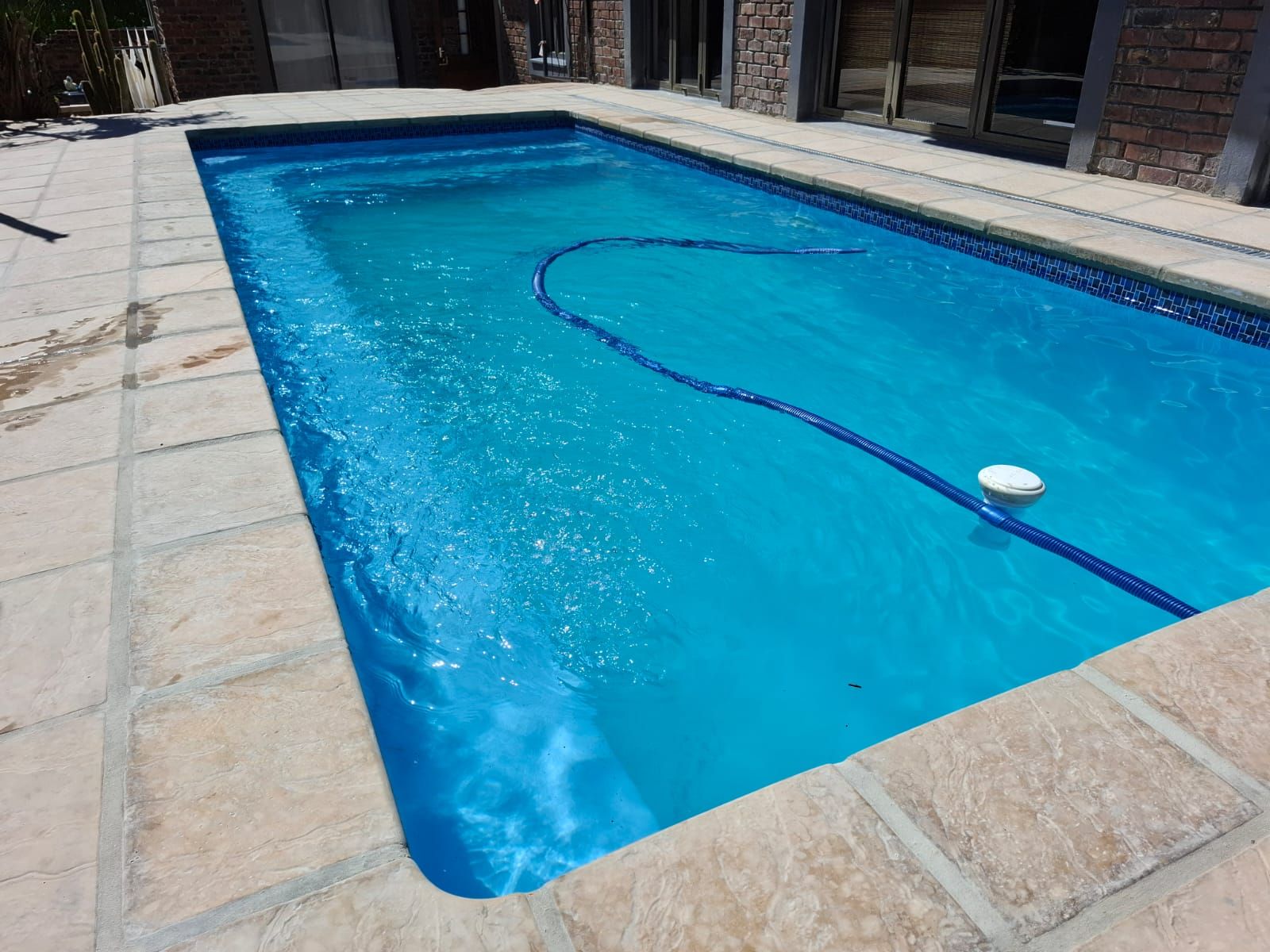 Piscina retangular com água azul límpida, rodeada por um deck revestido de azulejos.