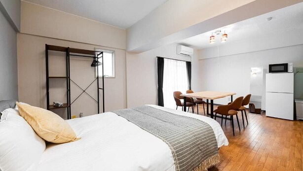 Quarto com cama, escrivaninha, cadeiras e uma kitchenette.