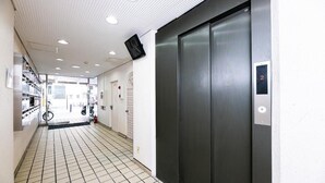 Um corredor com piso de azulejos, um elevador e uma porta com mostrador de número.