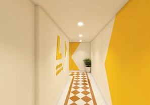Um corredor com piso xadrez, um vaso de plantas e uma parede com padrão geométrico e texto.