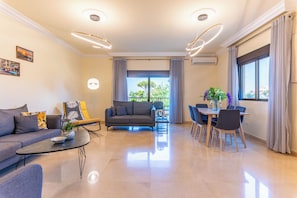 Uma sala de estar moderna com um sofá, uma mesa de jantar com cadeiras e uma varanda com cortinas.