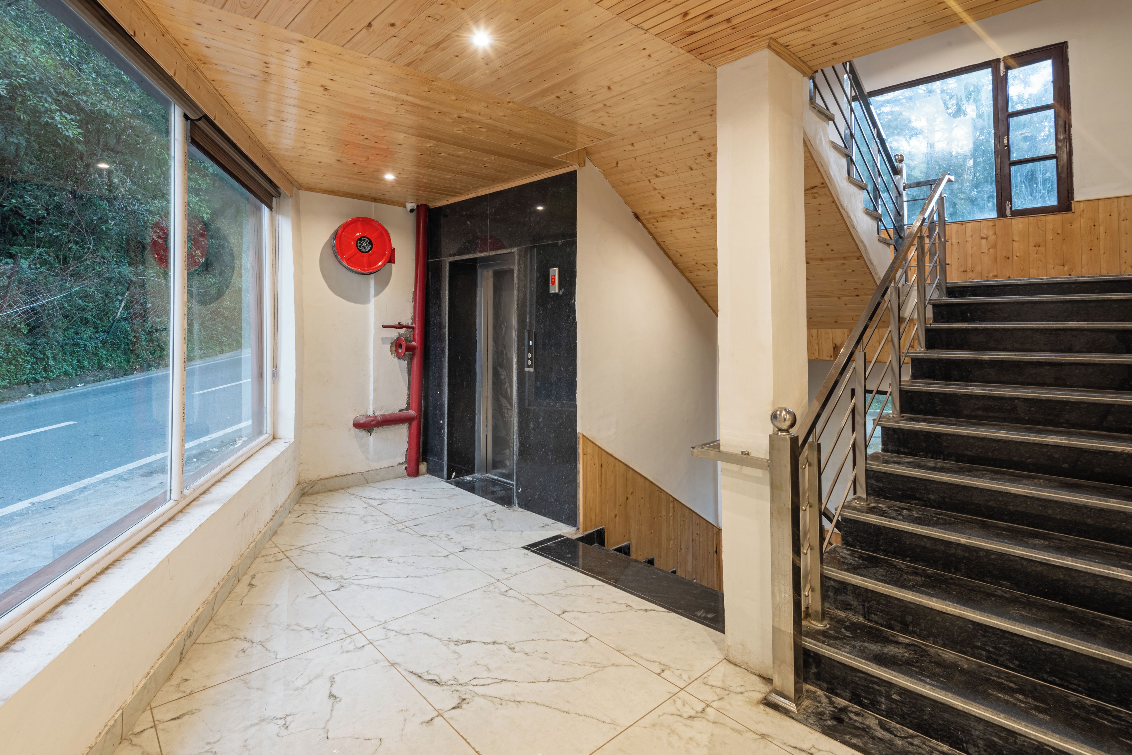 Um corredor com piso de mármore, um alarme de incêndio vermelho e uma escada com degraus de madeira.