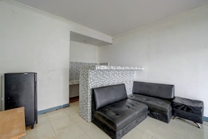 Um quarto com geladeira preta, sofá preto e lareira revestida de azulejos.