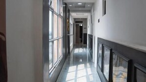 Um corredor comprido e estreito com chão de azulejos e grandes janelas em uma das laterais.