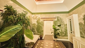 Um quarto com teto de madeira, um candelabro, uma porta branca e uma grande planta em vaso.