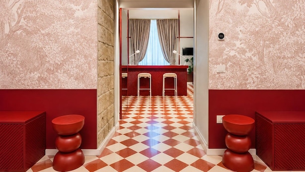 Um corredor com chão xadrez leva a um espaço de bar com banquetas e balcão.