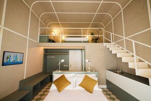Quarto de hotel com cama, escrivaninha, cadeira, escada e porta.