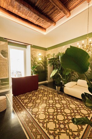 Um quarto com piso estampado, teto de madeira, um sofá, uma planta grande e uma parede com um mural de tema natural.