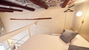Quarto com cama, luminária pendente e teto com vigas de madeira.