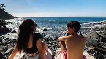 Duas pessoas sentadas numa praia rochosa, com o oceano ao fundo.