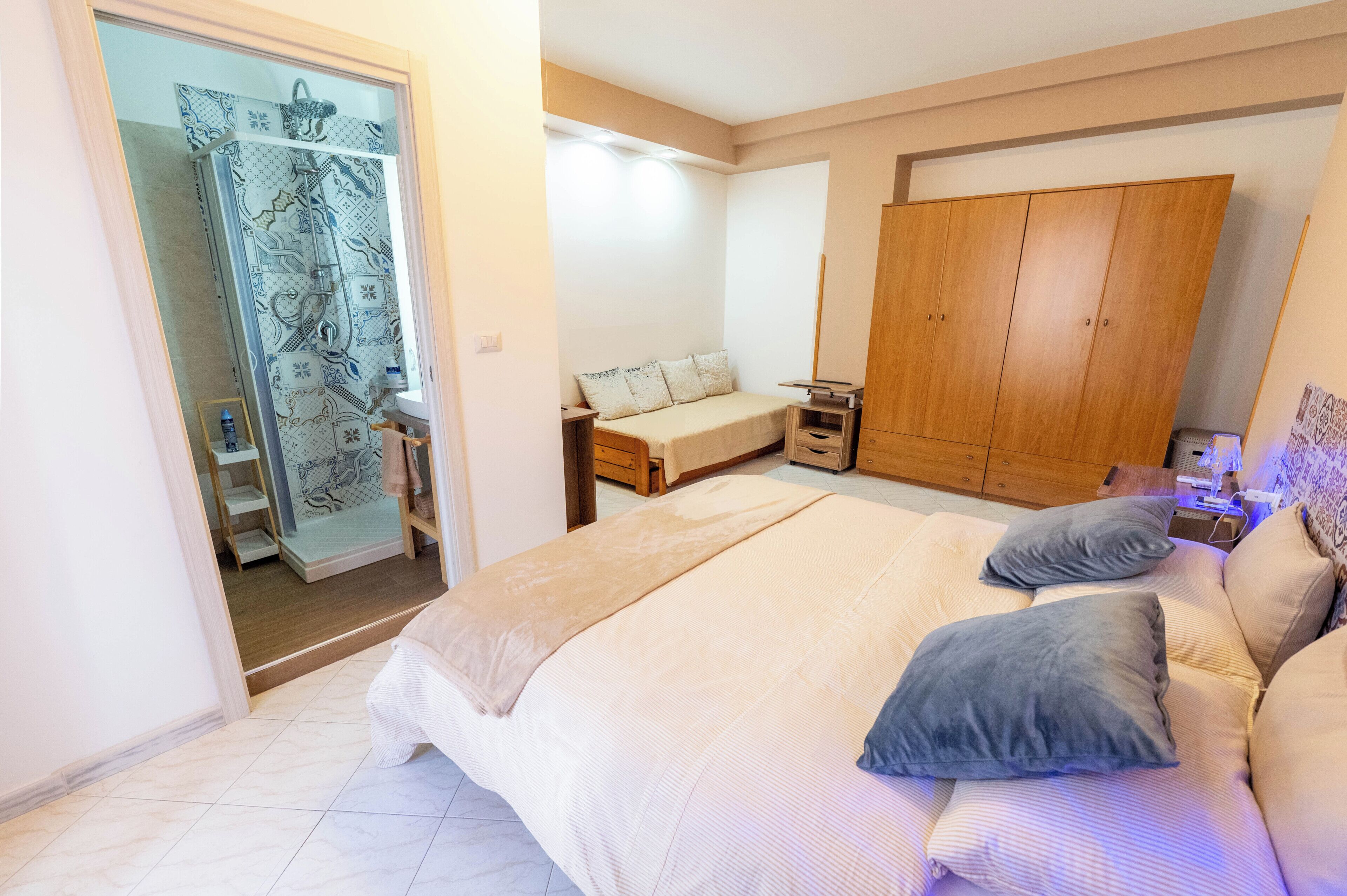 Um quarto com cama, mesas de cabeceira, guarda-roupa e banheiro com chuveiro.