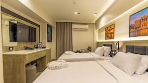 Quarto de hotel com duas camas, uma escrivaninha, um espelho, uma televisão e um quadro de uma ponte.