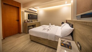 Quarto de hotel com cama de madeira, uma escrivaninha com computador, espelho e televisão.