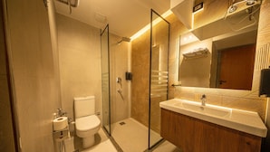 Casa de banho moderna com chuveiro em cabine de vidro, sanita e toucador com espelho.