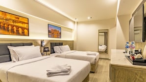 Quarto de hotel com duas camas, banheiro, escrivaninha com comodidades e obras de arte nas paredes.