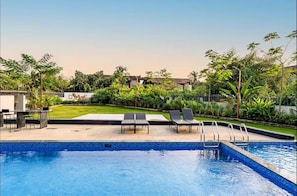 Piscina com espreguiçadeiras e um gramado bem cuidado.