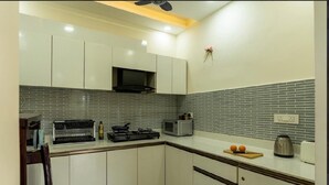 Uma cozinha com armários brancos, micro-ondas, chaleira e torradeira na bancada.