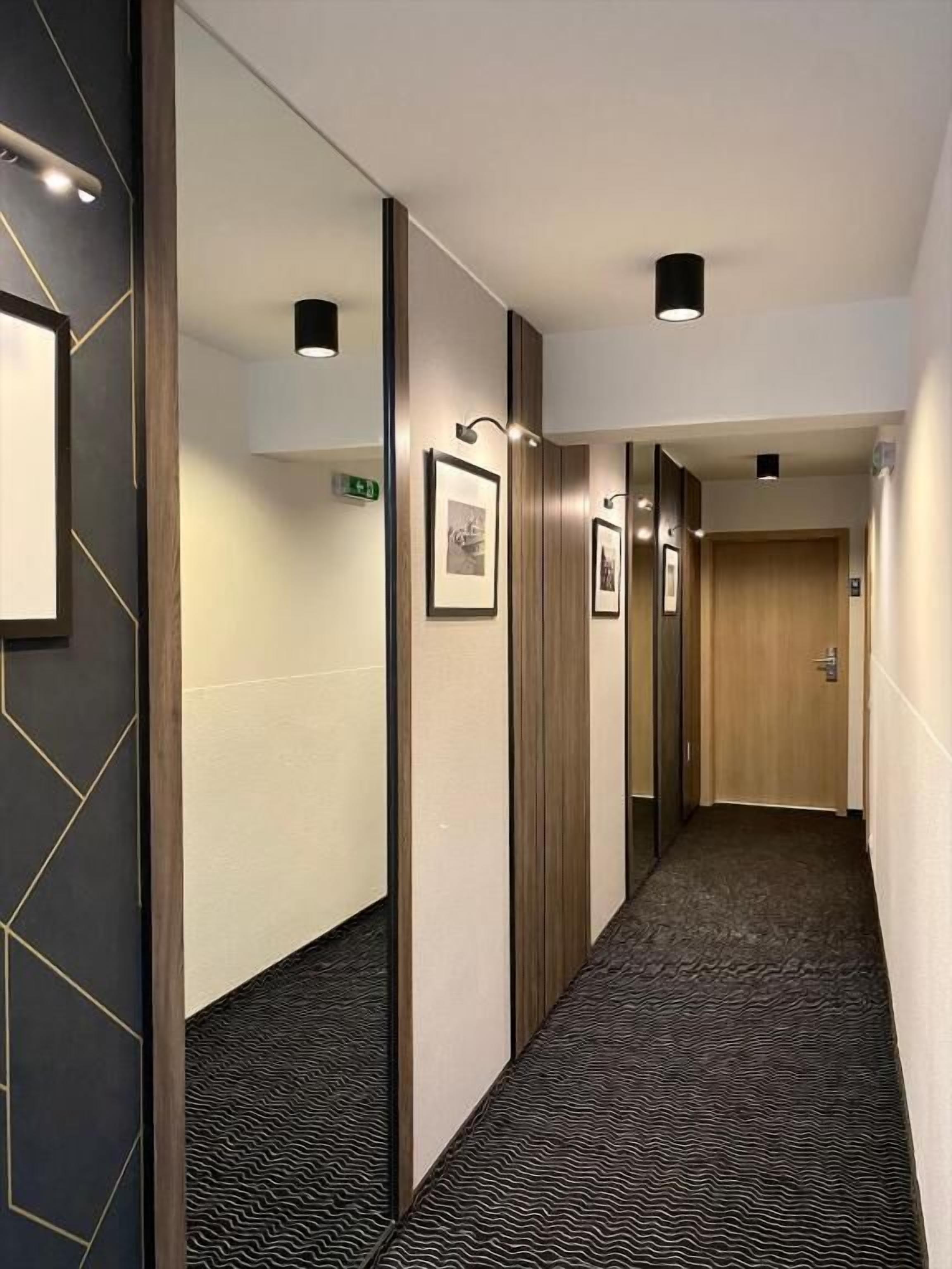 Um corredor com quadros nas paredes, piso coberto por carpete e uma porta de madeira no final.