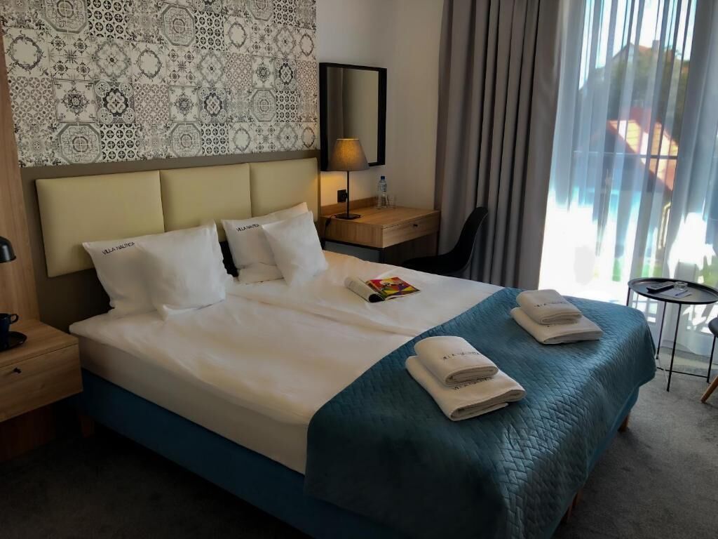 Quarto de hotel com uma cama, mesa de cabeceira, abajur, cadeira e uma pequena mesa.