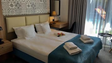 Quarto de hotel com uma cama, mesa de cabeceira, abajur, cadeira e uma pequena mesa.