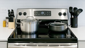 Cozinha com micro-ondas e fogão de aço inoxidável, armários brancos e painel de azulejos.
