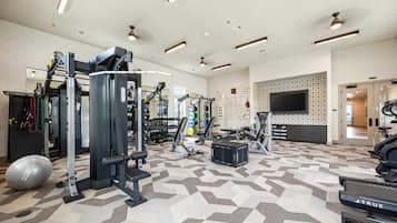 Uma academia com diversos equipamentos de exercício, piso estampado e uma televisão na parede.