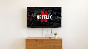Uma televisão na parede com o logotipo da Netflix, um armário de madeira abaixo e uma pequena planta em cima do armário.