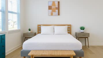 Quarto bem arrumado com cama, mesas de cabeceira, um banco e uma obra de arte na parede.