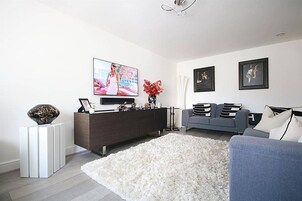 Uma sala de estar moderna com uma televisão de tela plana, um armário de madeira escura, um sofá cinza e um tapete felpudo branco.